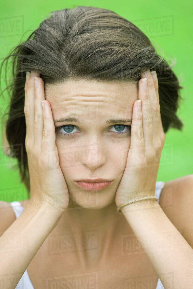 Teen girl holding face in hands, furrowing brow, close-up - Royalty ...