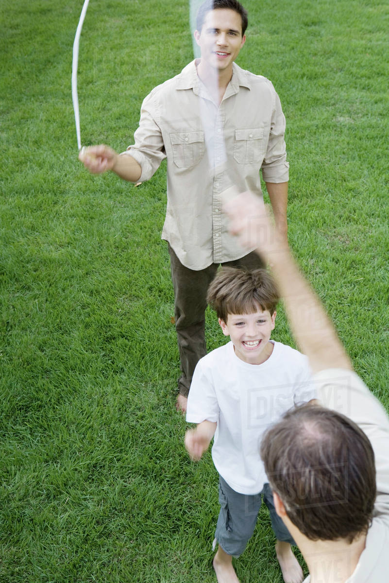 Boy playing jump rope with two men, smiling, cropped view - Royalty ...