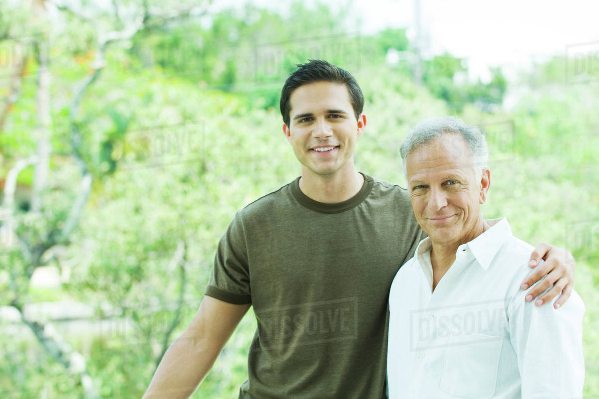 Young man with arm around his father's shoulder, both smiling at camera ...