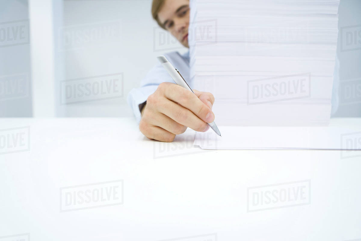 Man sitting behind tall stack of documents, writing on single sheet of ...