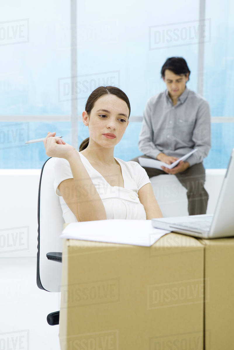 Young woman sitting at cardboard box desk, looking at laptop computer ...