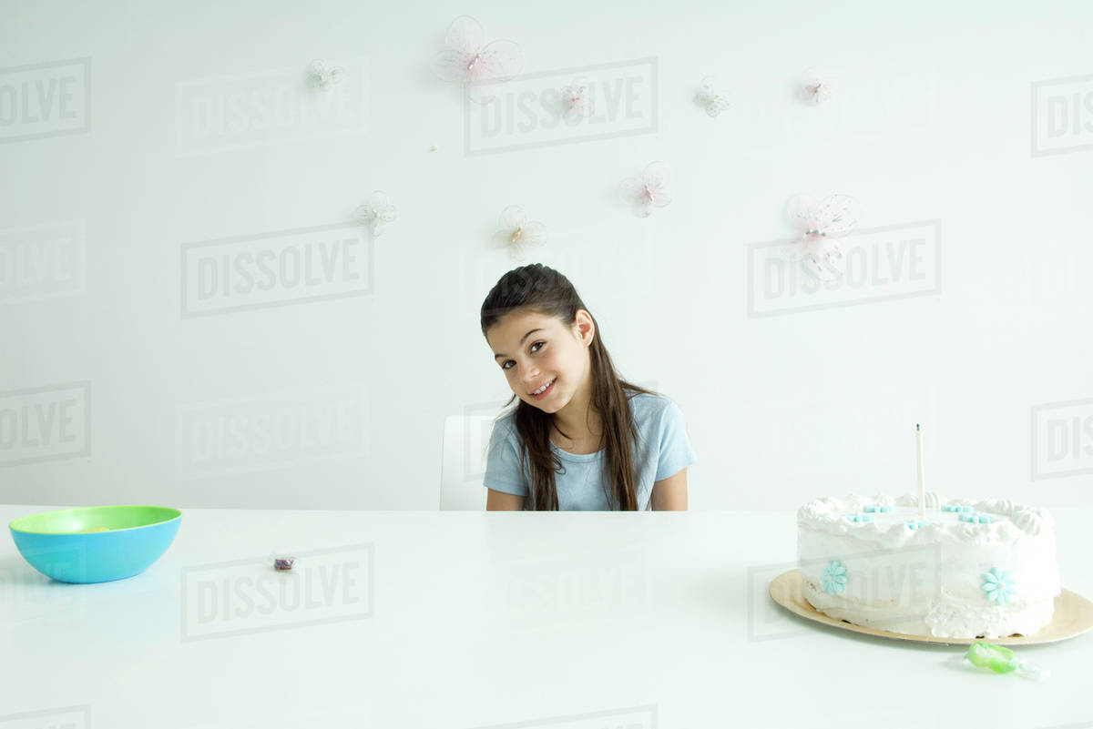 Girl sitting at table with birthday cake, smiling at camera - Royalty ...