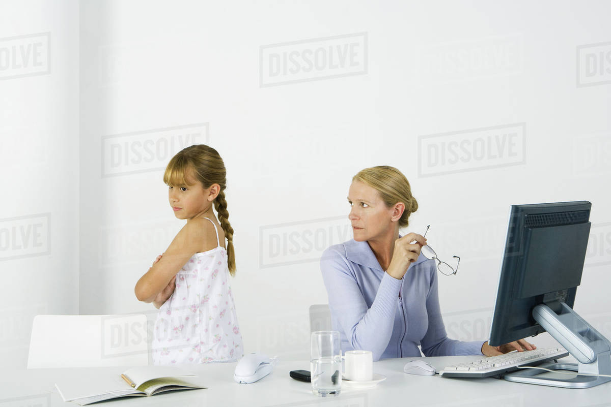 Woman sitting before computer, looking over shoulder at daughter ...