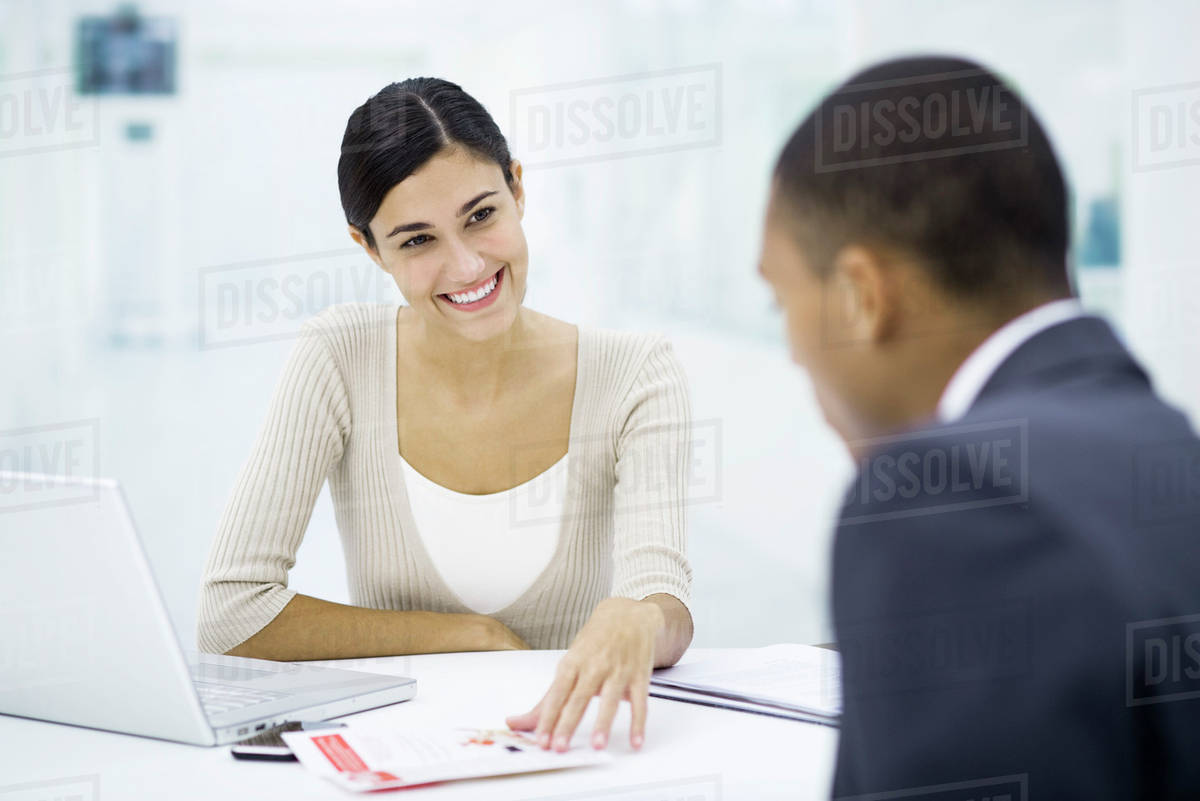 Professional woman sitting with client at desk, discussing brochure ...