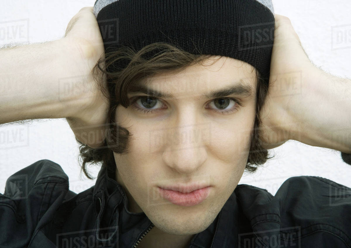 Young man with hands on side of head, looking at camera, close-up ...