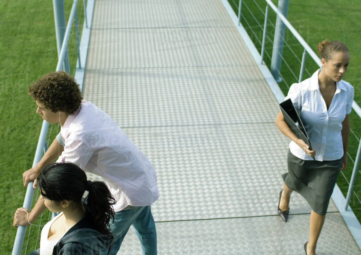 Teenage couple leaning against rail of walkway while businesswoman ...
