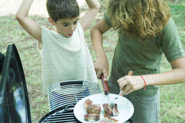 Boy cutting up meat on plate while second boy watches - Royalty-free ...