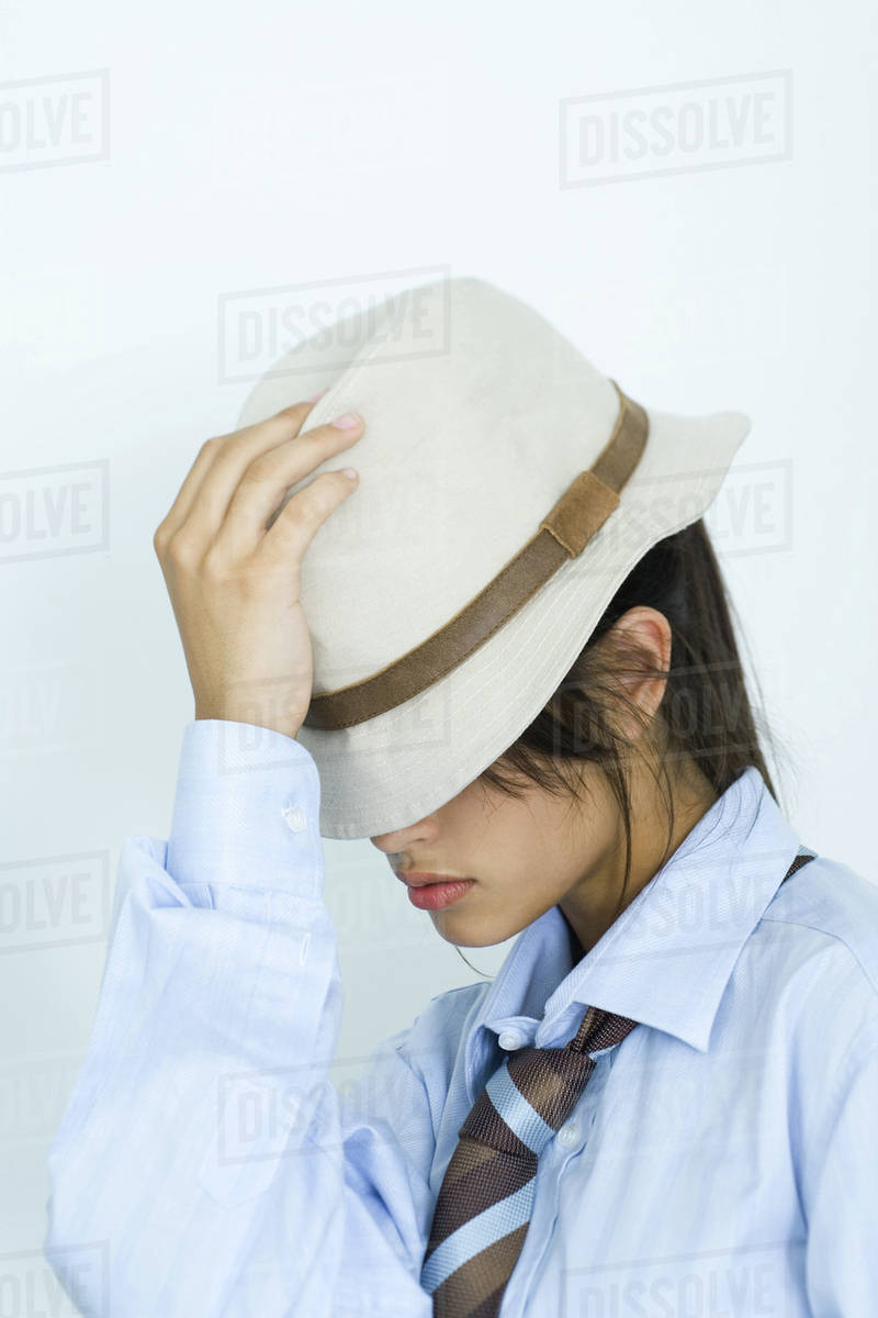 Teen girl wearing shirt, tie, and hat, pulling hat down over eyes ...