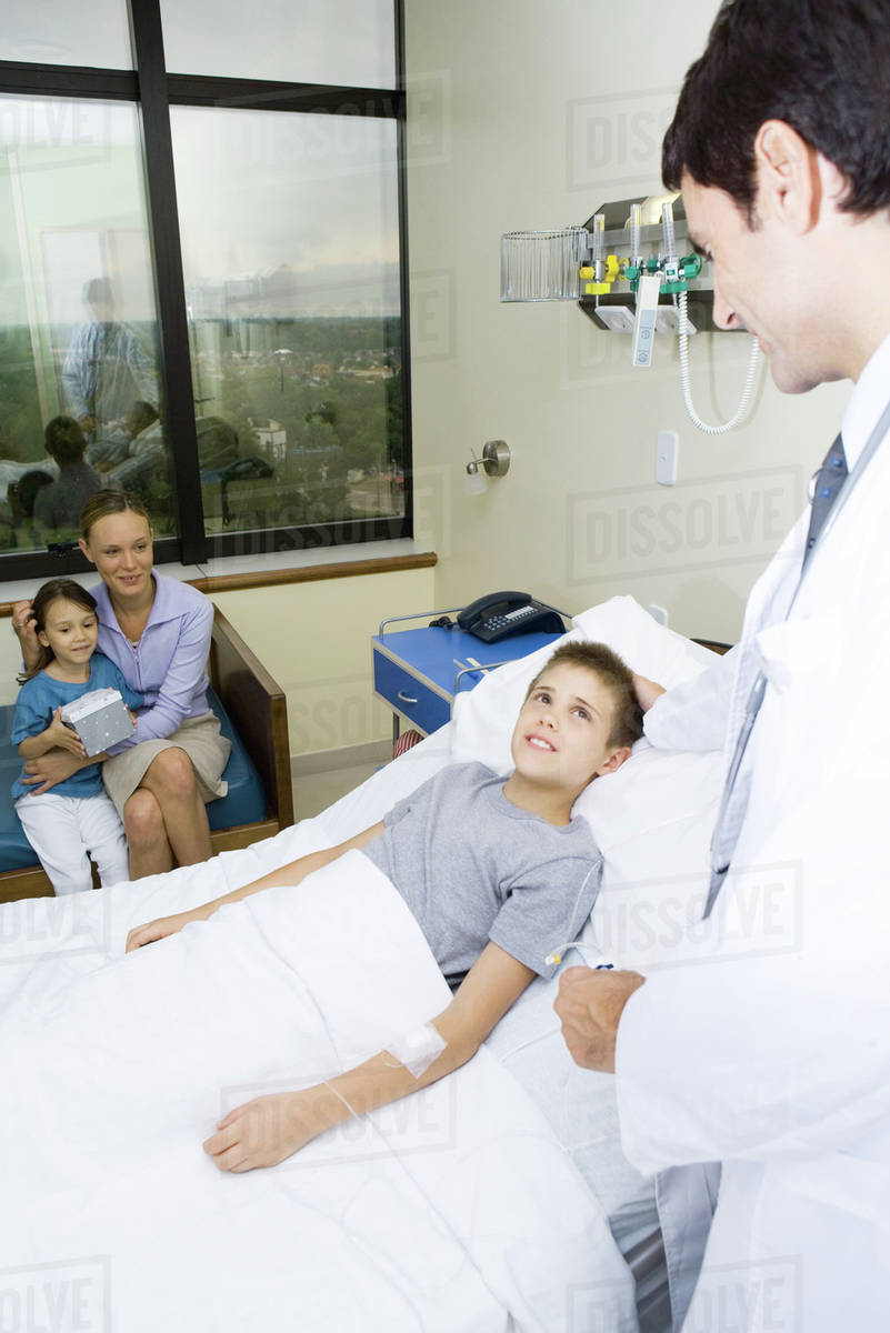 Boy lying in hospital bed surrounded by family and doctor - Royalty ...