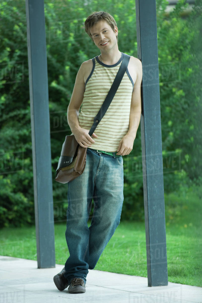 Man standing leaning against post, smiling, full length portrait ...