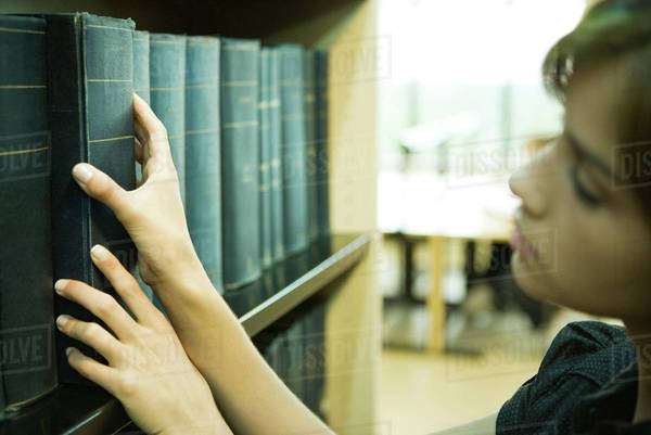 Female student taking reference book from shelf in library - Royalty ...