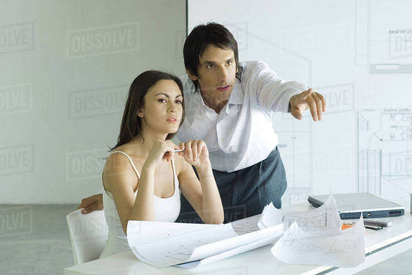 Couple next to table with blueprints, man leaning over woman's shoulder ...