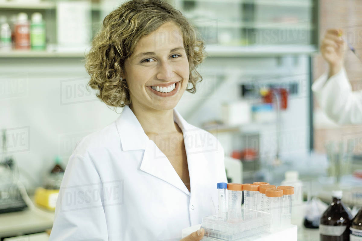 Female lab worker holding rack of empty test tubes, smiling at camera ...