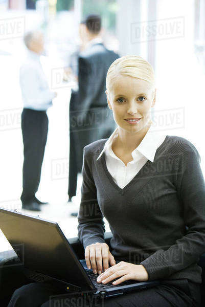 Young woman sitting, using laptop computer, smiling at camera - Royalty ...