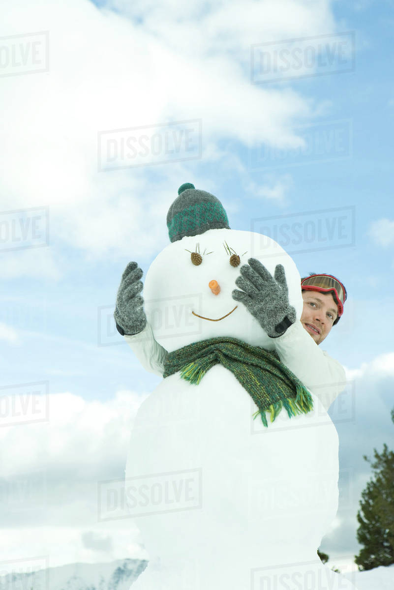 Young man embracing snowman, looking around, portrait - Stock Photo ...