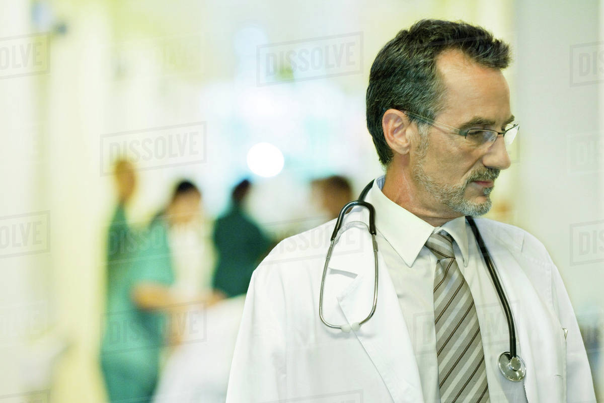 Male doctor looking away, head and shoulders, hospital corridor in ...