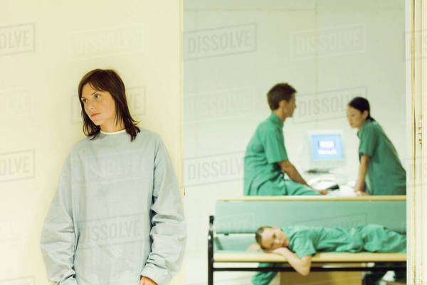 Female patient standing in hospital corridor, medical staff in office ...