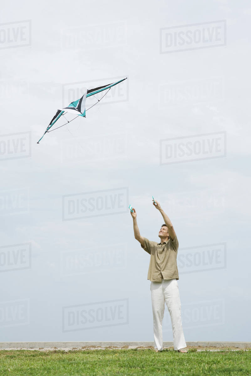 Man flying kite, arms raised, full length - Stock Photo - Dissolve