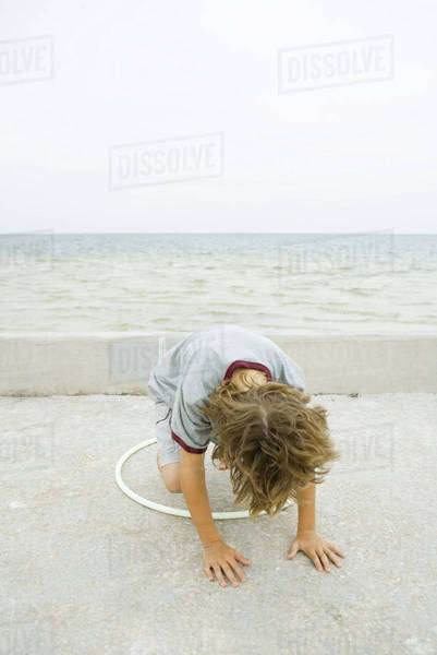Boy crouching on all fours, playing with plastic hoop, head down ...
