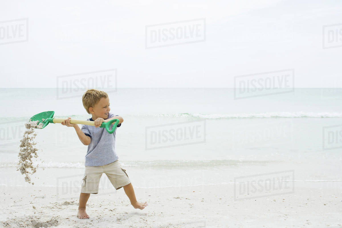 Young boy at the beach, holding up shovel and spilling sand - Royalty ...
