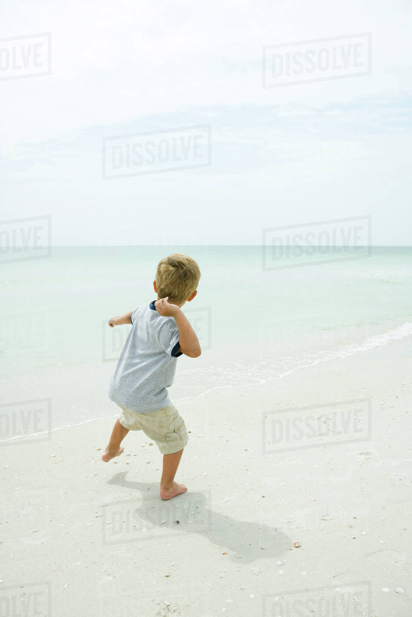 Boy on beach throwing unseen object toward ocean, rear view, full ...