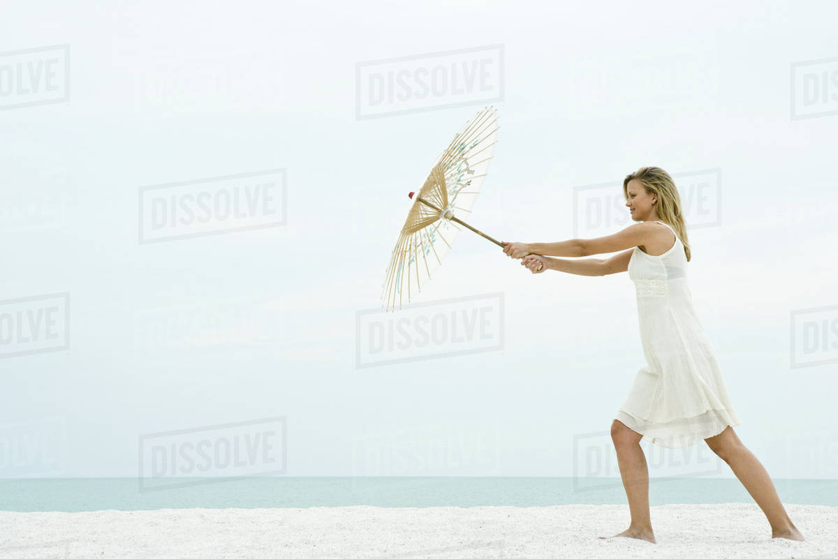 Woman holding parasol on beach, full length - Stock Photo - Dissolve