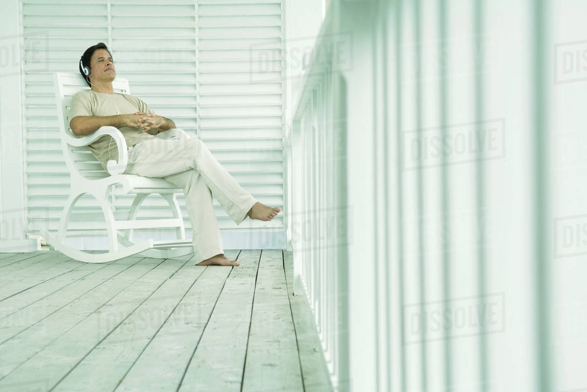 Man sitting in rocking chair on porch, listening to headphones ...