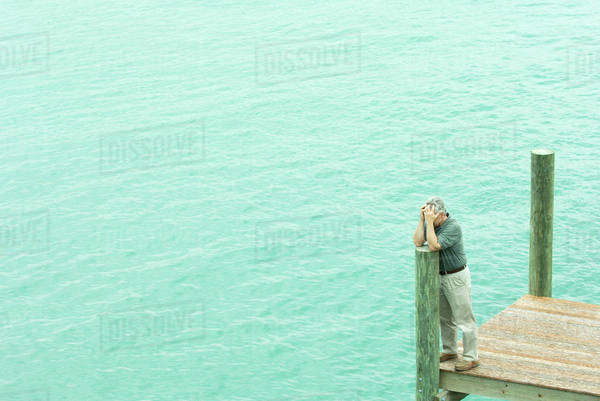 Man standing on dock, leaning on post, holding head, high angle view ...