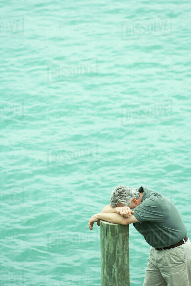 Man leaning on post, head down on arms, high angle view, water in ...