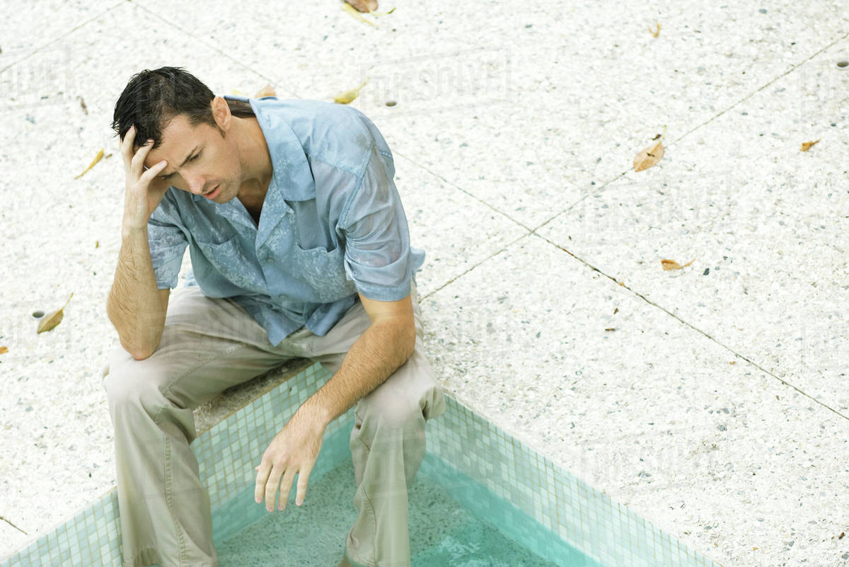 Man sitting with feet in pool, holding head, high angle view - Royalty ...