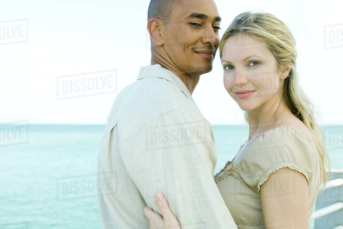 Couple embracing, both smiling at camera, ocean in background - Royalty ...