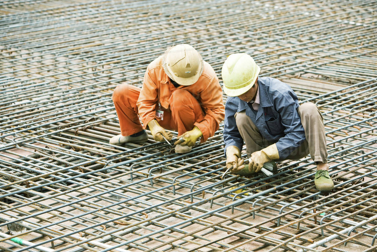 Construction workers crouching on steel framework, both looking down ...