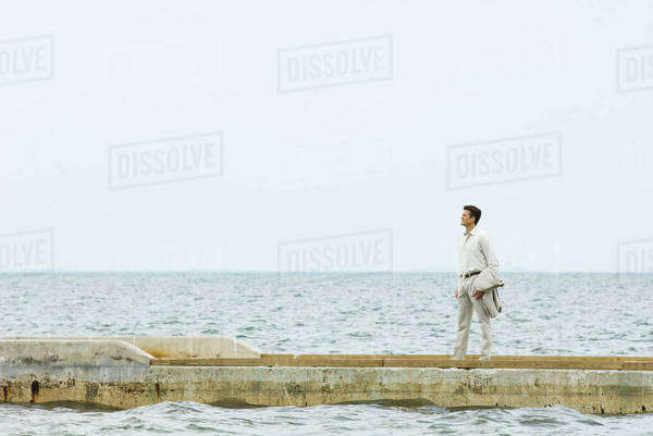 Man standing on jetty, looking at sea, in mid distance - Royalty-free ...
