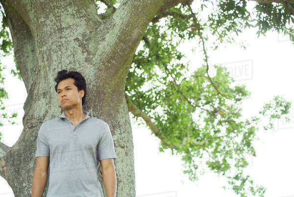 Man leaning against tree, looking away, waist up - Royalty-free Stock ...