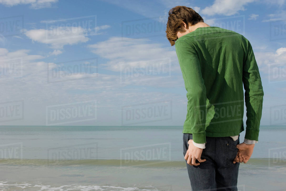 Young man standing on beach with head down, rear view - Royalty-free ...