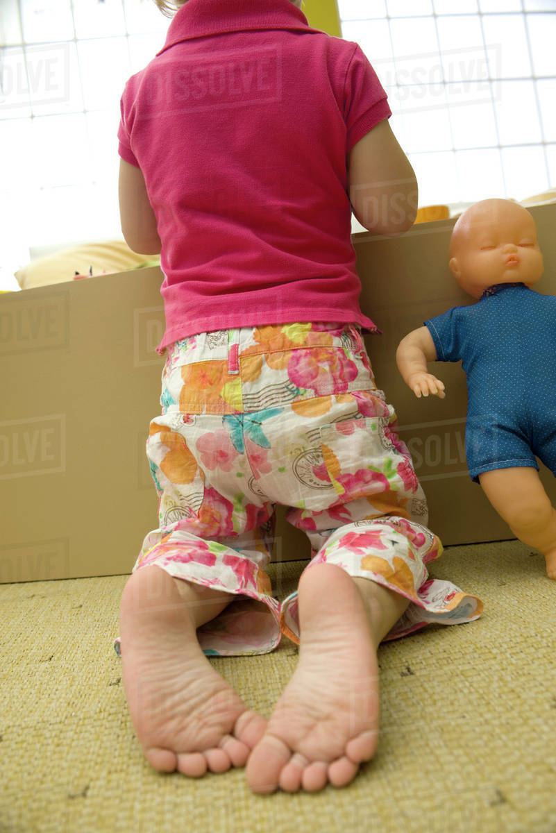 Little girl kneeling before box of toys, rear view - Stock Photo - Dissolve
