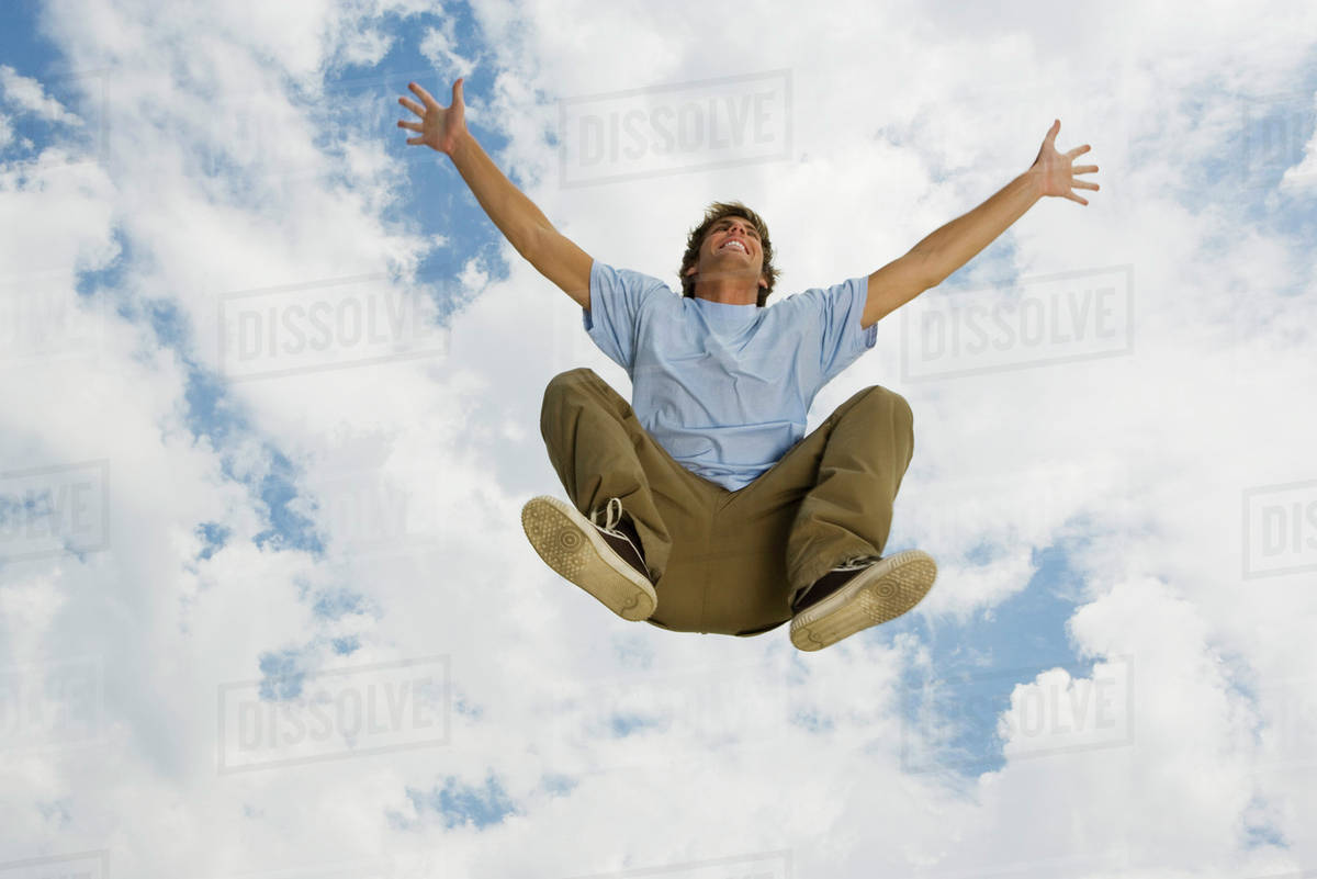 Young man jumping in midair, low angle view - Stock Photo - Dissolve