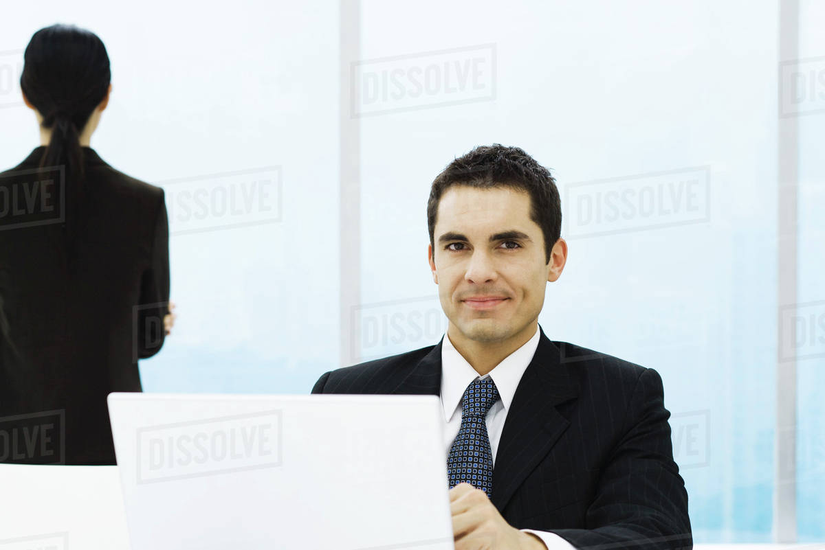 Businessman sitting behind computer screen, smiling at camera - Royalty ...