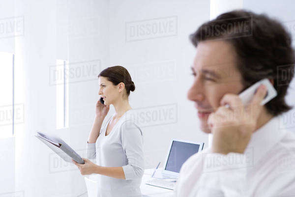 Business people in office using cell phones - Stock Photo - Dissolve
