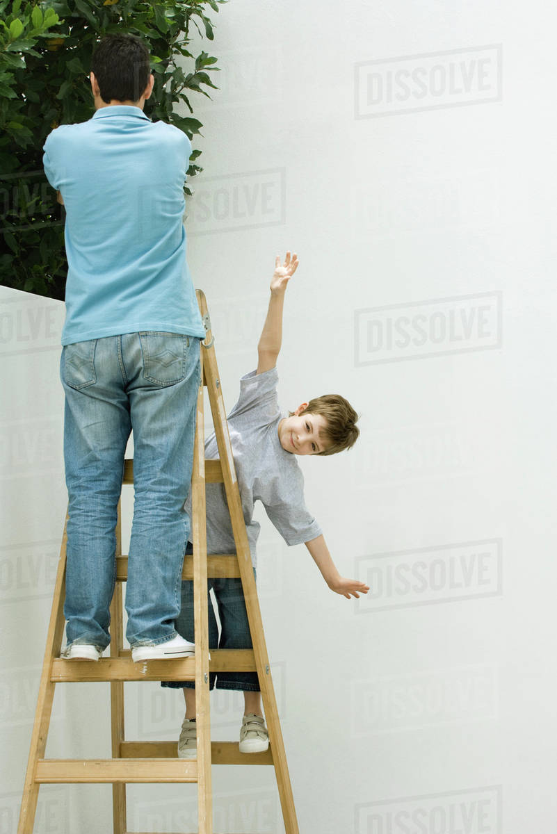 Father and son standing on ladder, boy pretending to be a plane ...
