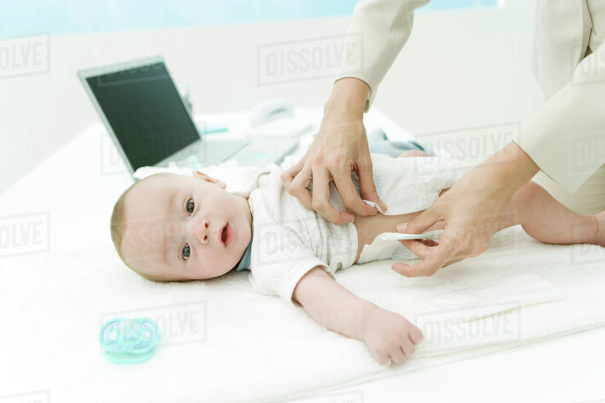 Mother changing baby's diaper on desk, laptop computer in background ...