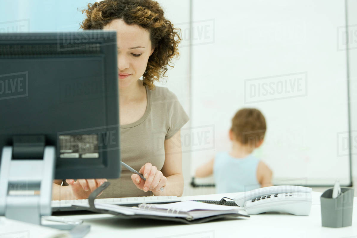 Woman working at computer in home office, young son playing in ...