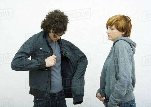 Young man and woman standing, man putting on jacket while woman watches ...