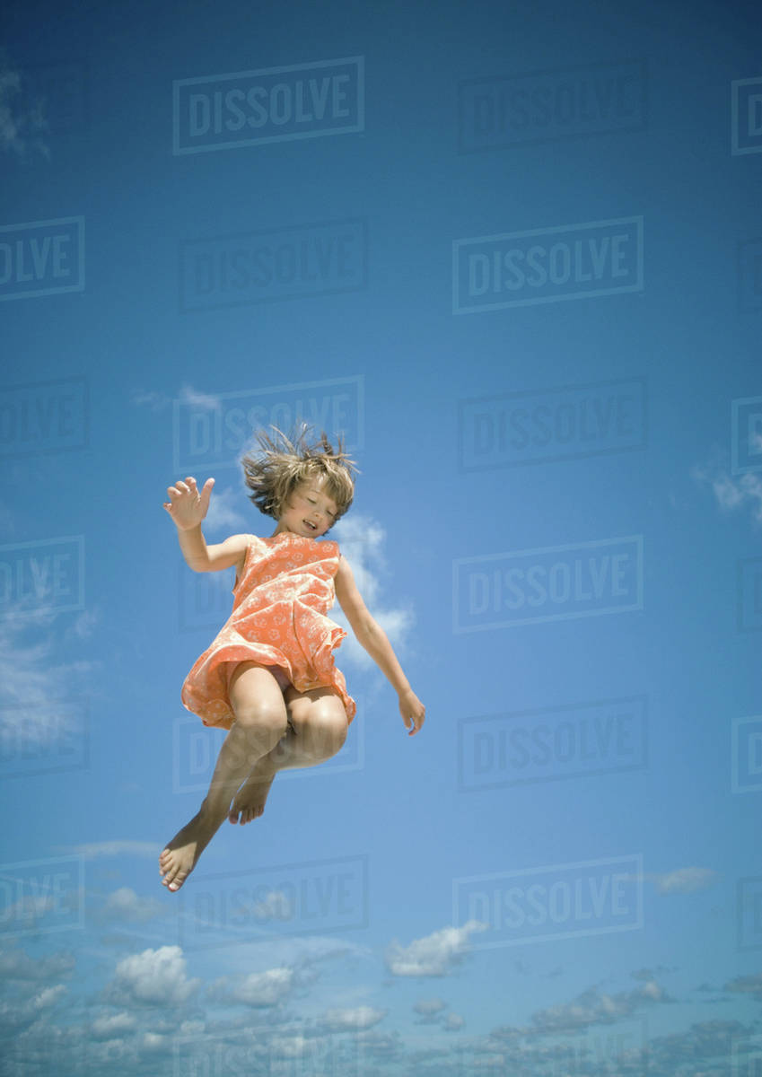 Girl jumping, sky in background, low angle view - Stock Photo - Dissolve