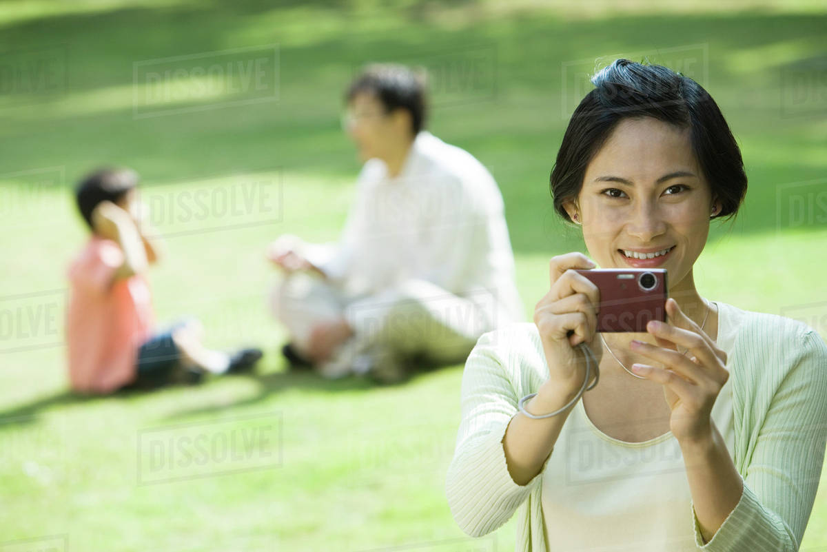 Woman aiming digital camera, smiling at camera - Stock Photo - Dissolve