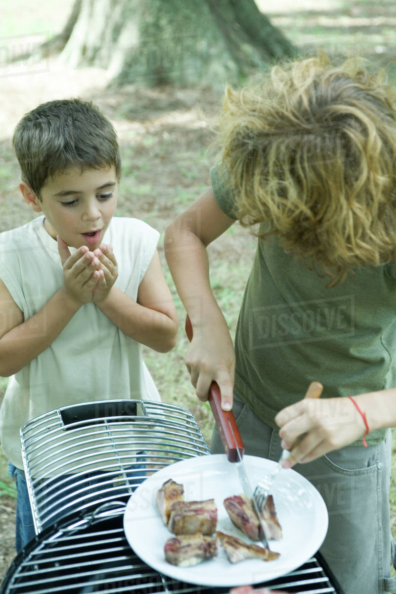 Boy cutting up piece of grilled meat while second boy watches - Royalty ...