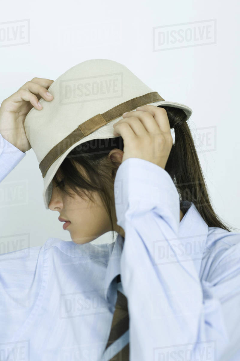 Teenage girl wearing shirt and tie, pulling hat down over eyes ...
