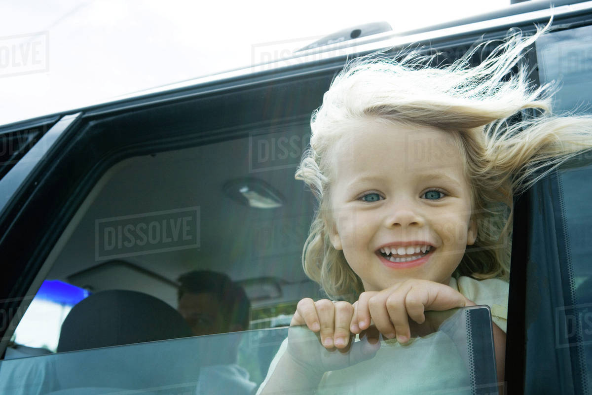 Little girl in car, looking out of window, smiling at camera, hair ...