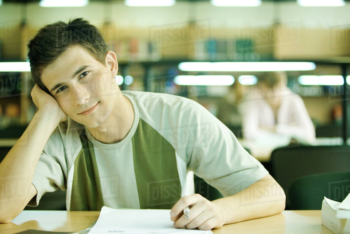 Male college student sitting in library, smiling at camera - Royalty ...
