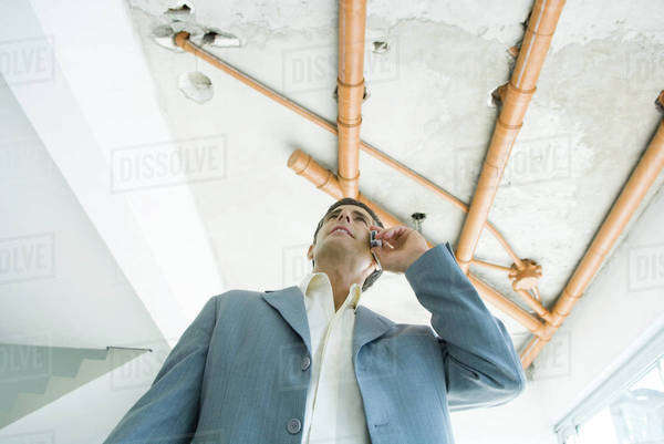 Man in suit using cell phone, bare pipes overhead, low angle view ...
